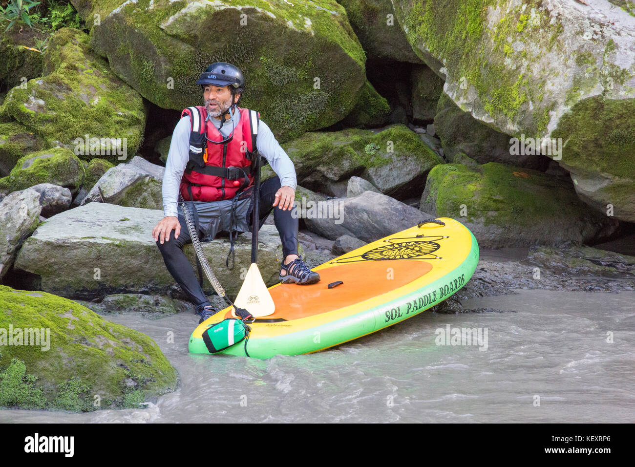Man rests with his stand-up paddleboard (SUP) while on jungle river ...