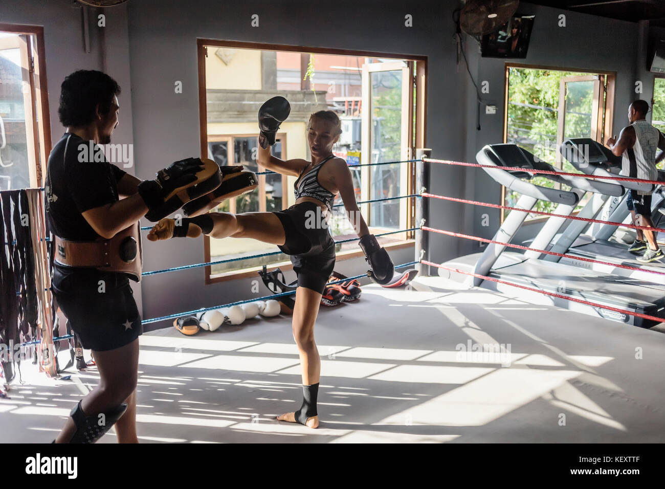 Photograph of young woman kicking while practicing kickboxing with ...