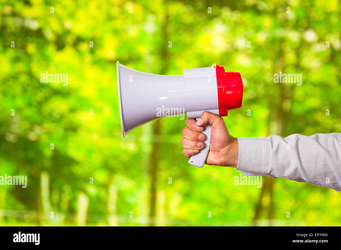 Handsome man holding in his hand a megaphone with a blurred green ...