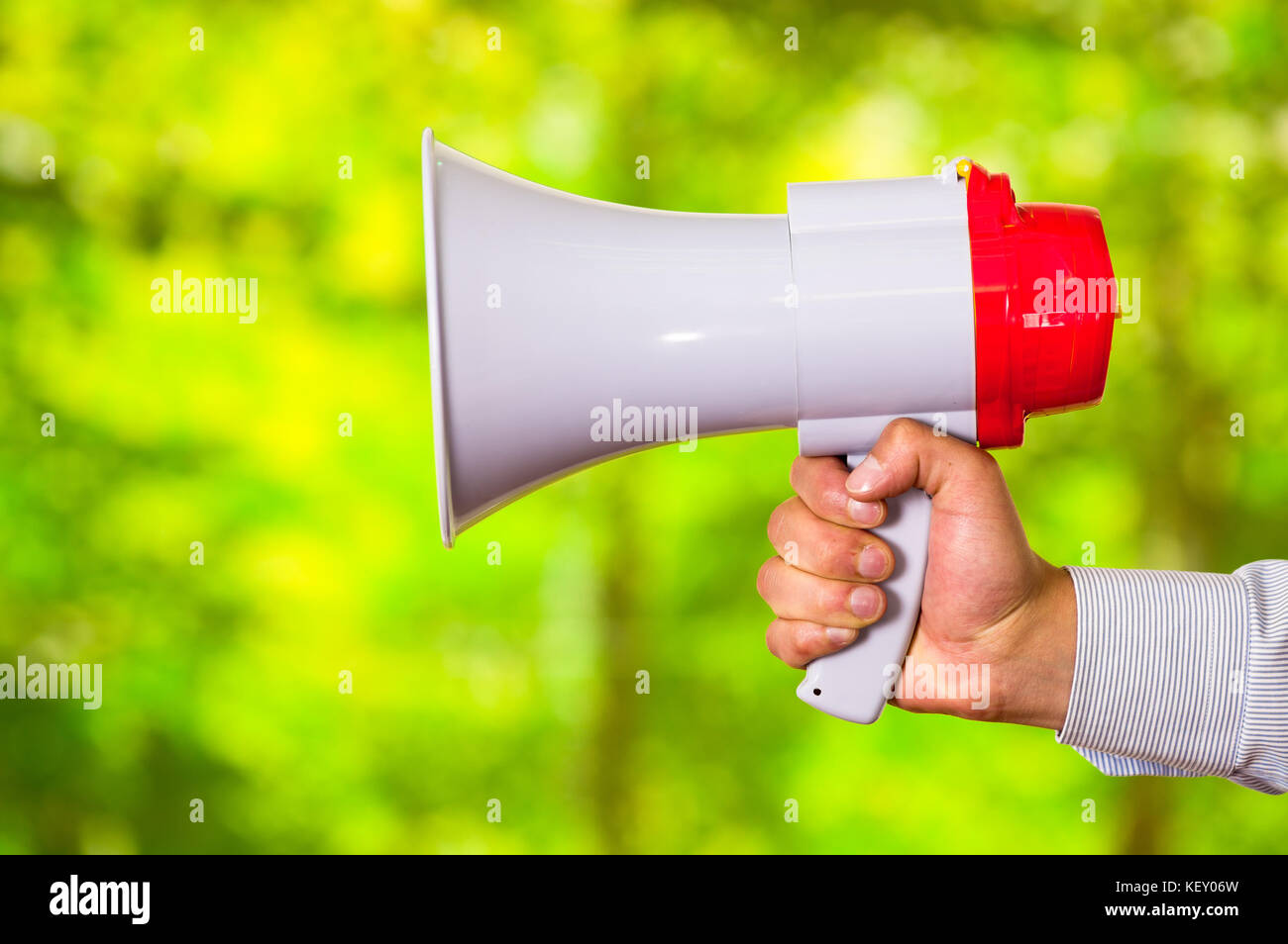 Handsome man holding in his hand a megaphone with a blurred green ...