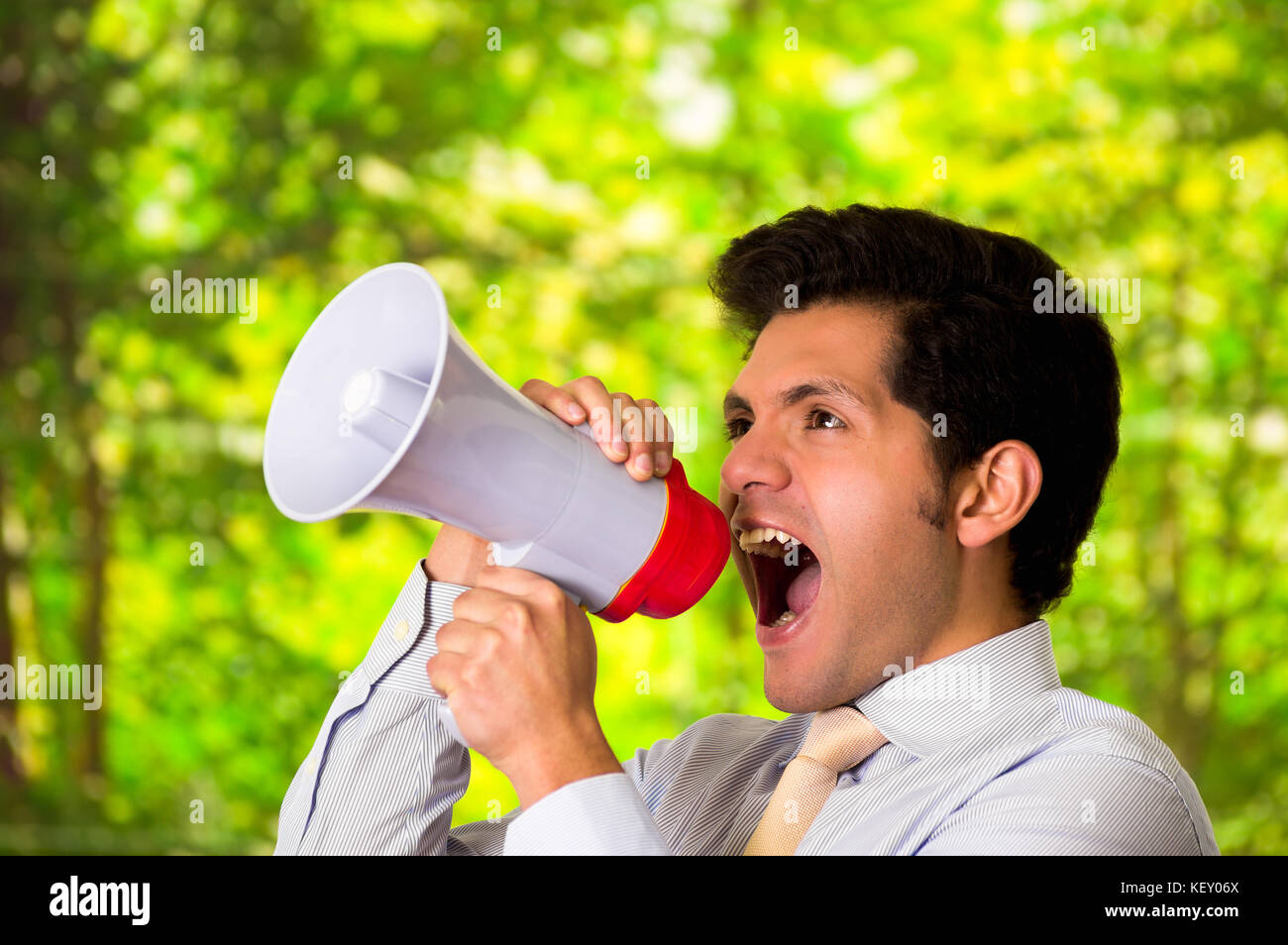 Portrait of a handsome man shouting with a megaphone in a blurred green ...