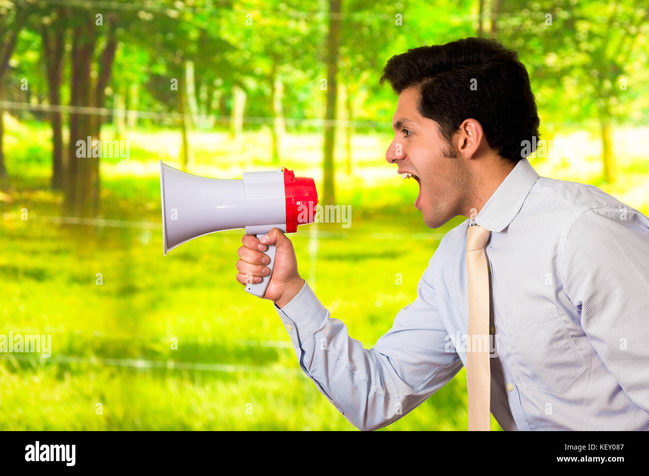 Portrait of a young man screaming with a megaphone, in a blurred green ...