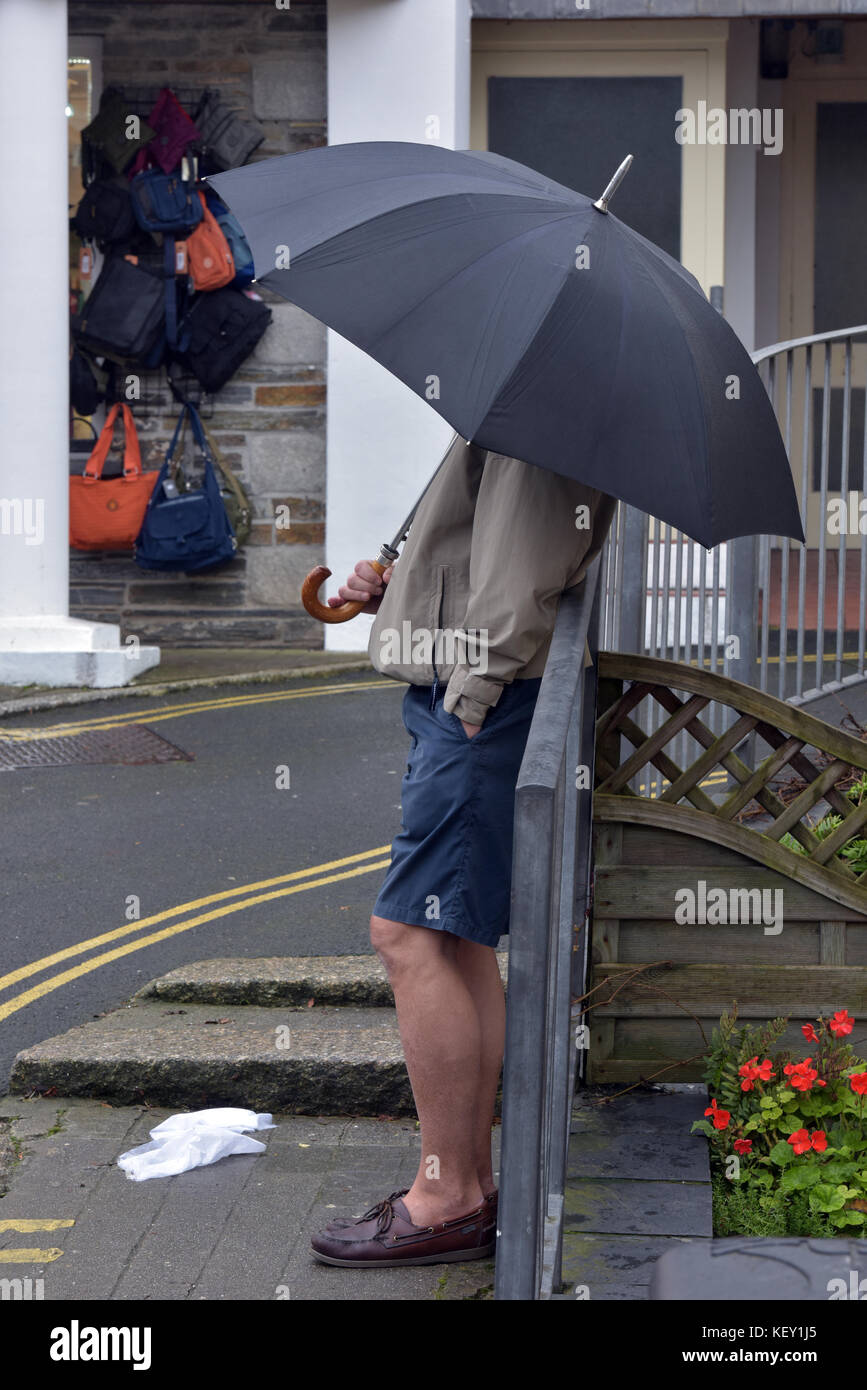 A man sheltering from the rain under or using a large grey umbrella ...