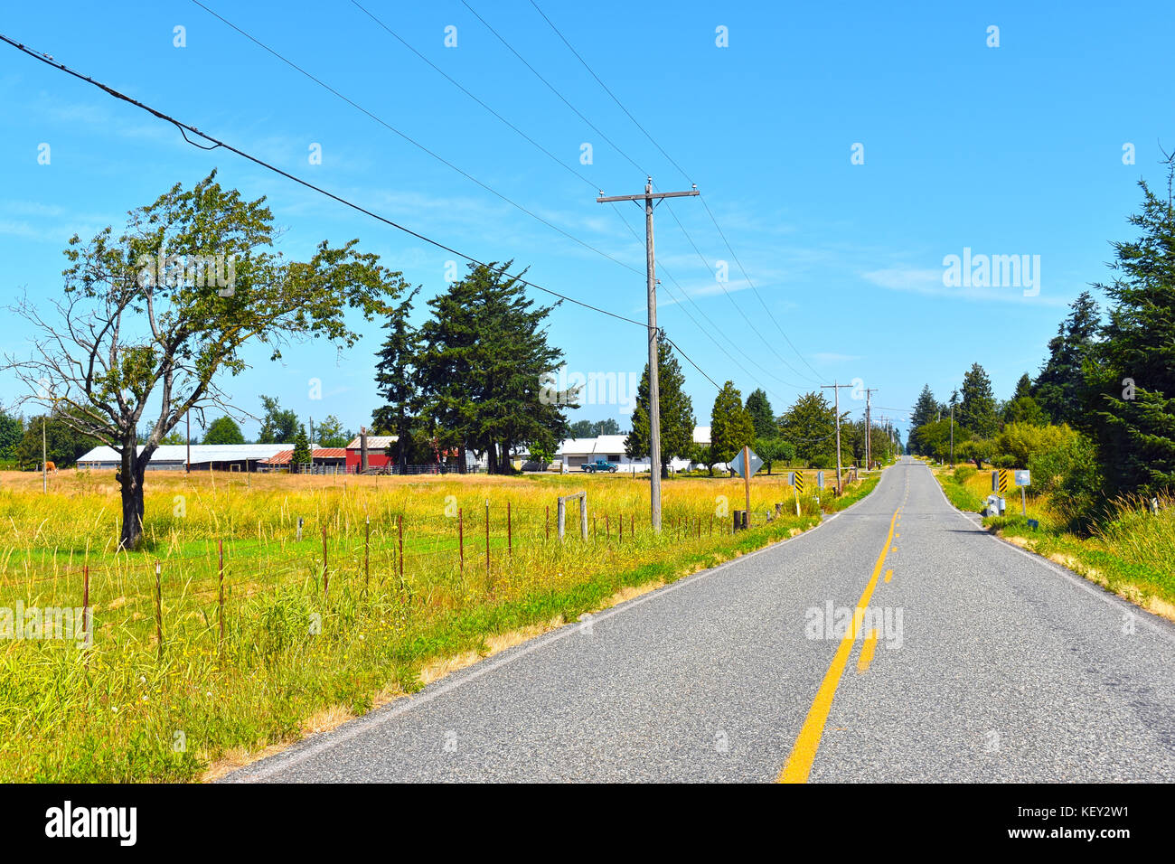 A long road in the country on a beautiful sunny day with a farm on the ...