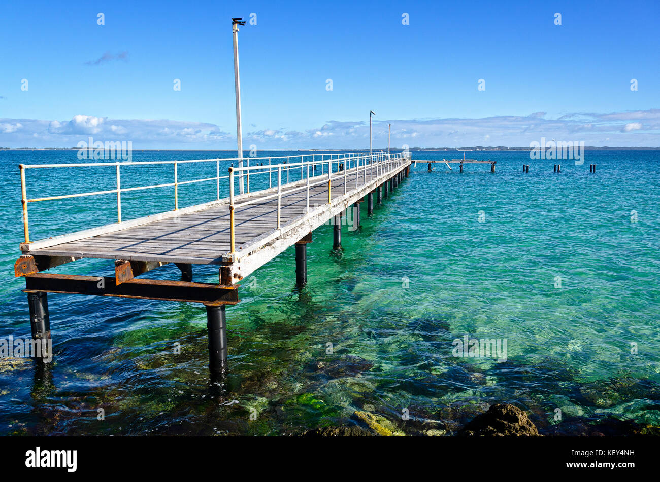 Disused damaged wooden jetty over sandy bottom with clear water and ...