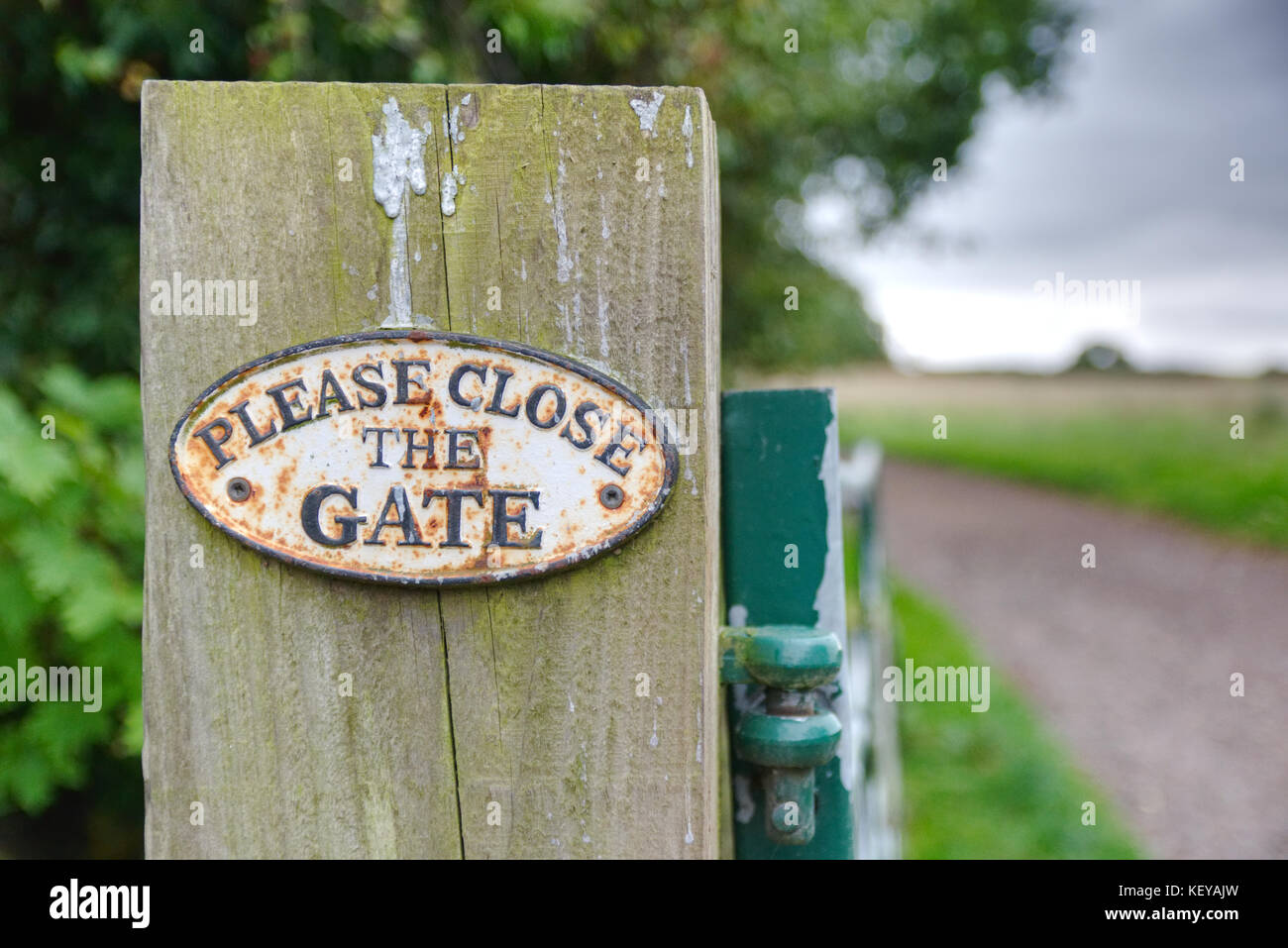 Weathered old Please Close The Gate sign on wooden post with path in ...