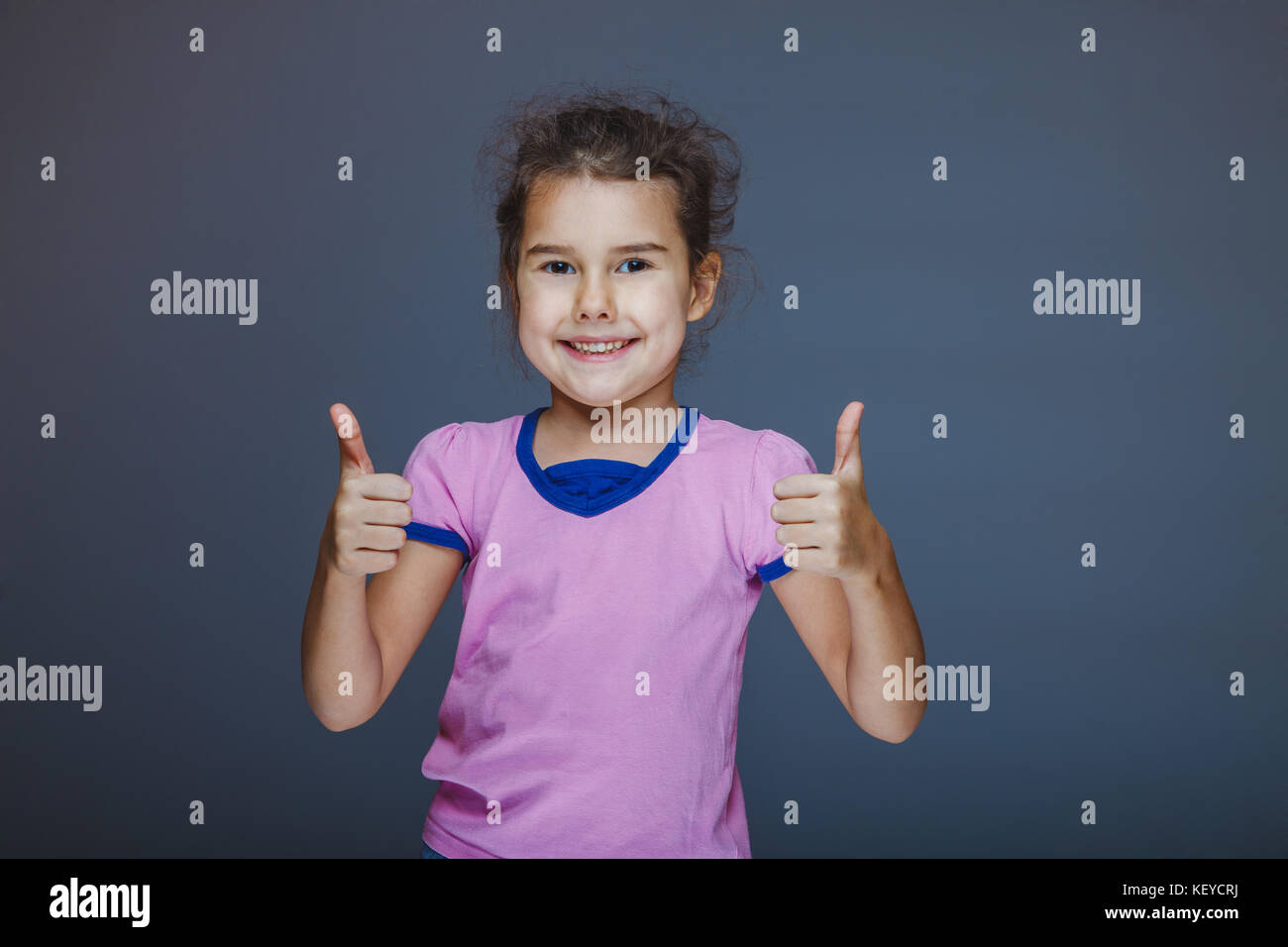 Girl showing thumbs up sign yes on a gray background Stock Photo - Alamy