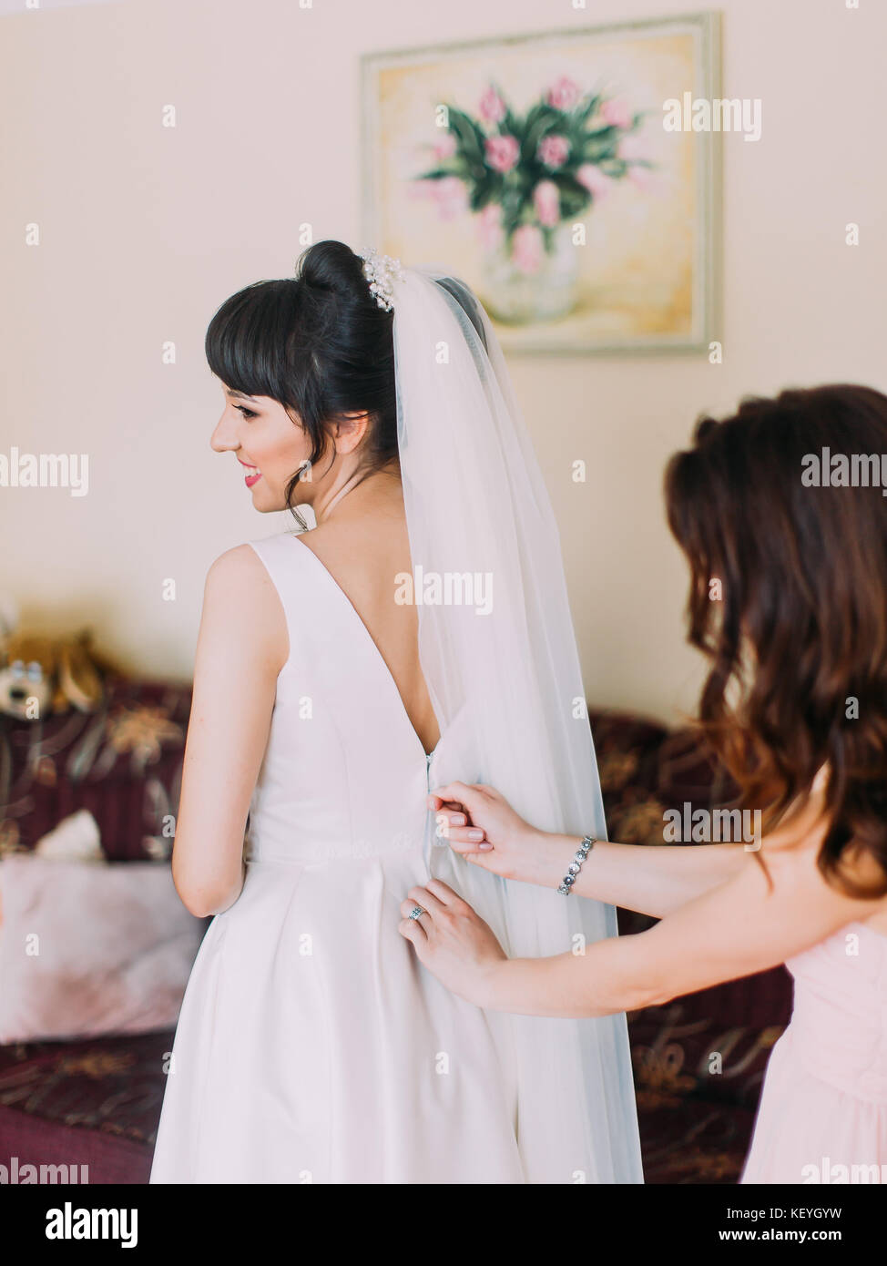 The bridesmaid is helping the bride with the wedding dress. Back view ...