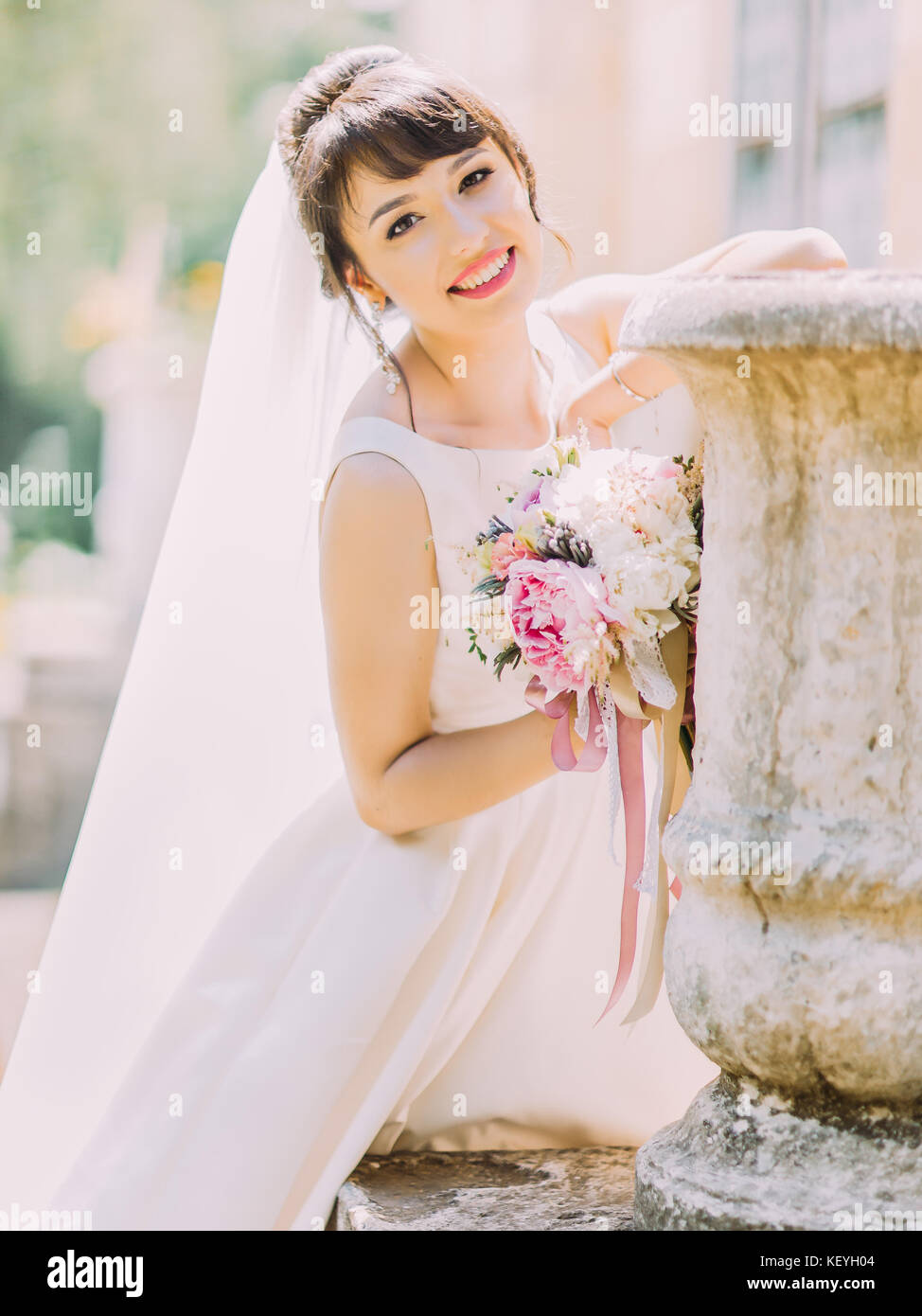 The smile of charming bride with the wedding bouquet leaning on the old ...