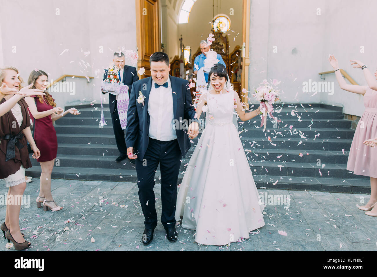 Happy newlyweds are leaving the church under the confetti Stock Photo ...