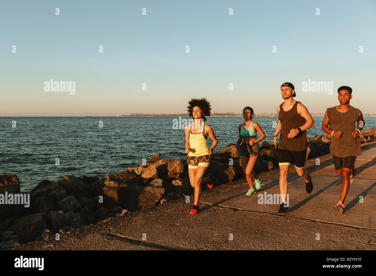 Full length image of four sports people running outdoors at the beach ...