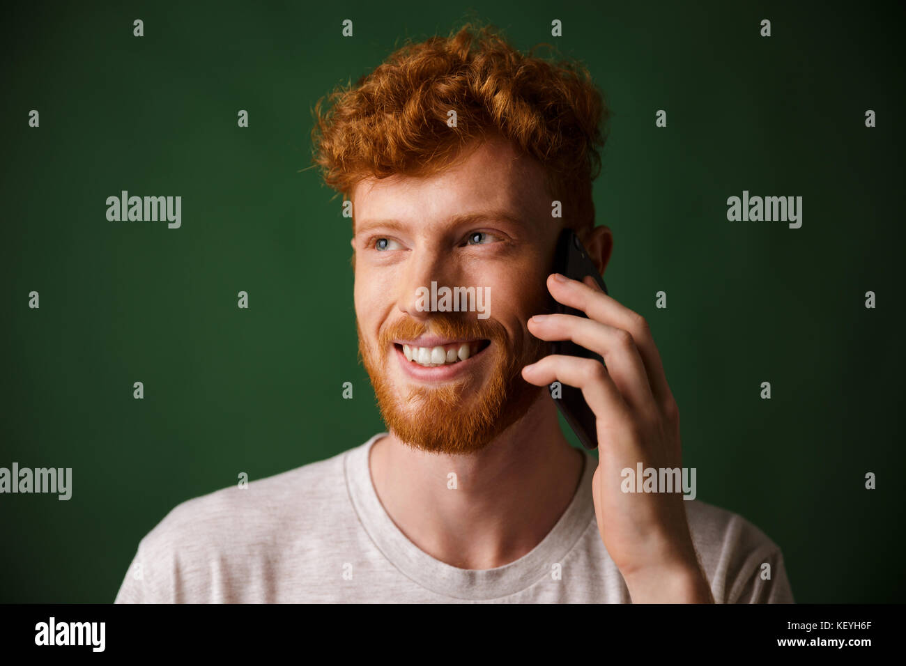 Handsome redhead bearded man talking on phone, over green background ...