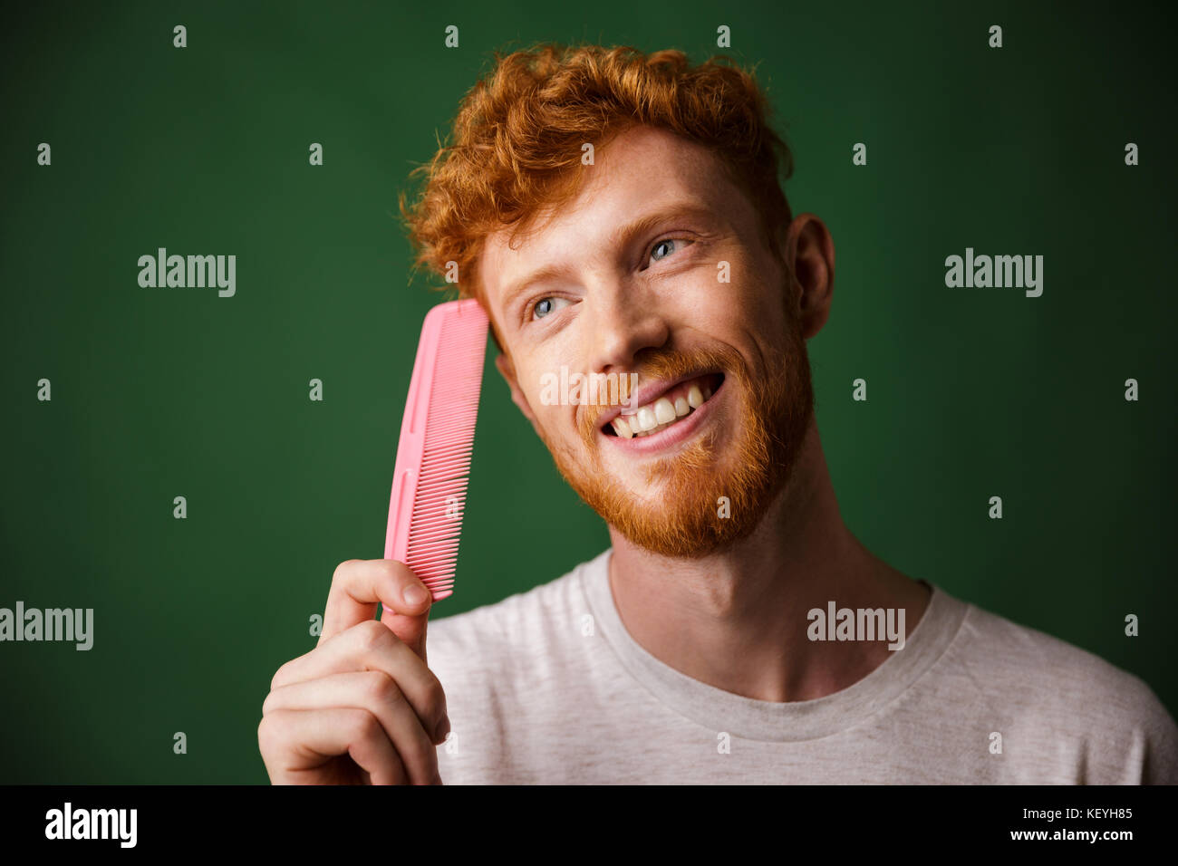 Close-up portrait of smiling young readhead beardy man with pink comb ...