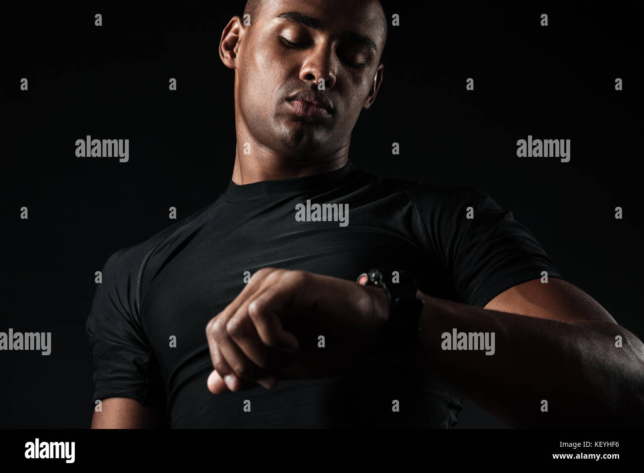 Young african muscular man looking at watch, over black background ...