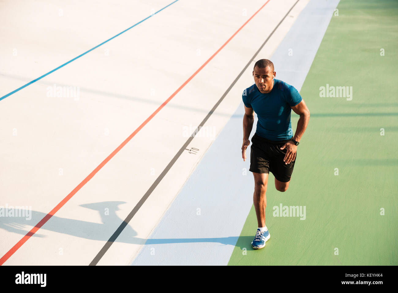Full length portrait of a muscular sportsman running on a track field ...