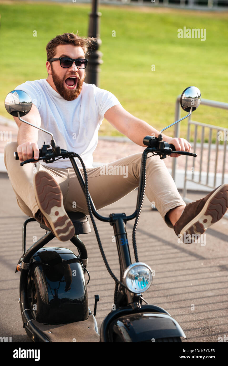 Vertical image of scared screaming bearded man in sunglasses rides on ...