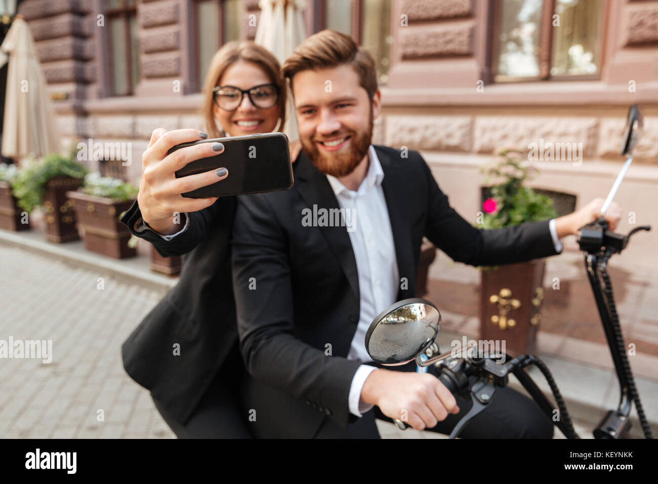 Cheerful stylish couple satting on modern motorbike outdoors and making ...
