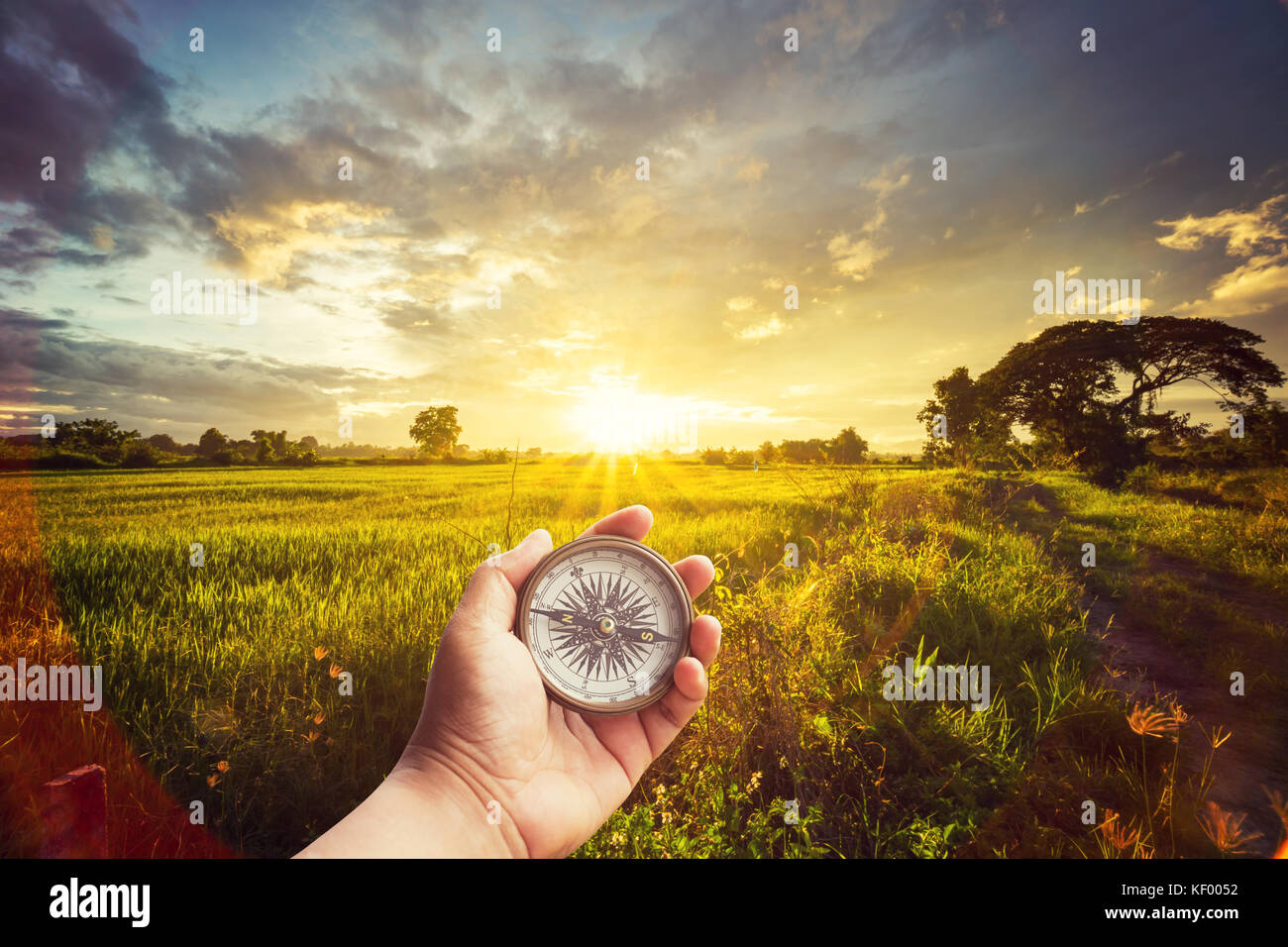 A man holding compass on hand at field and sunset for navigation guide ...