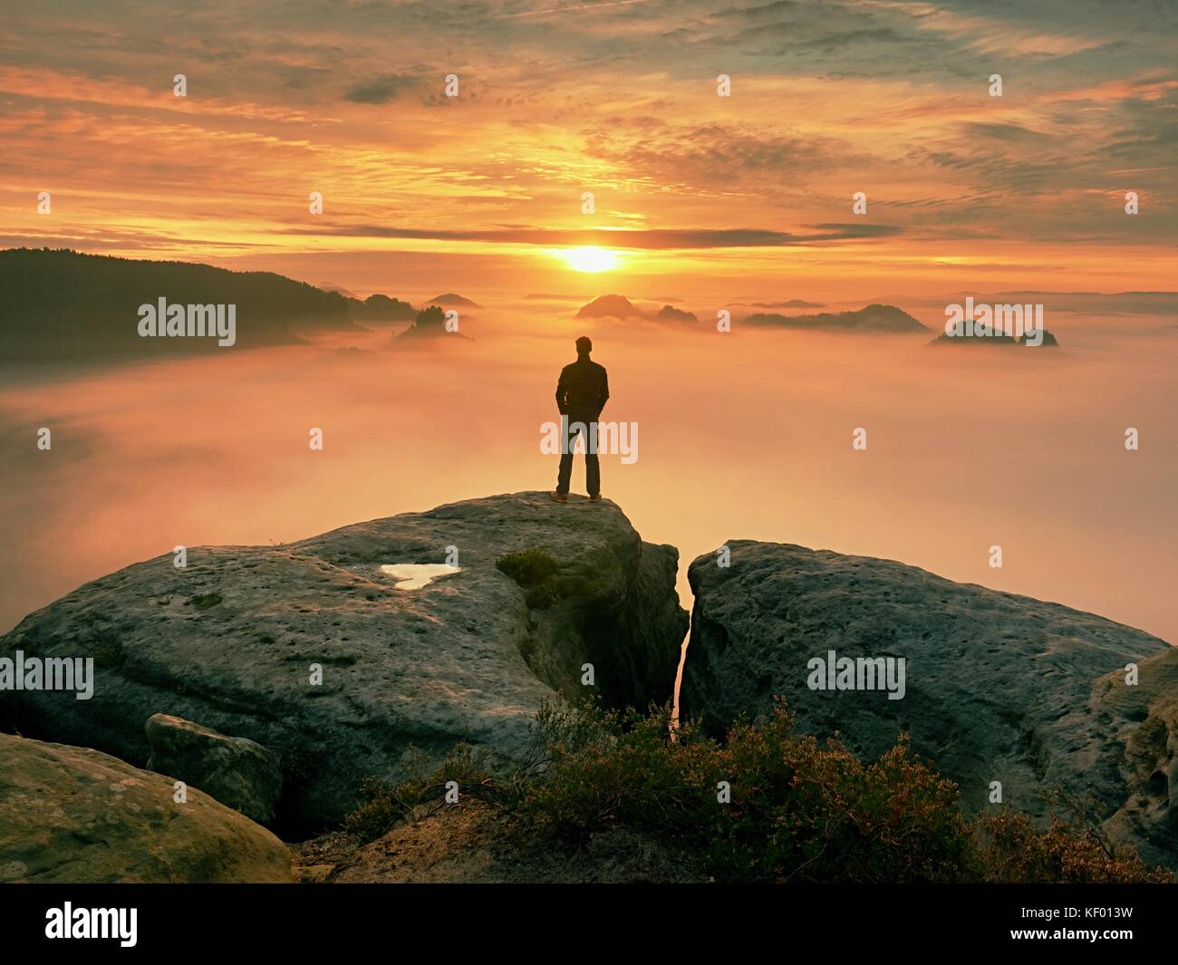 Man stands alone on the peak of rock. Hiker watching to autumn Sun at ...