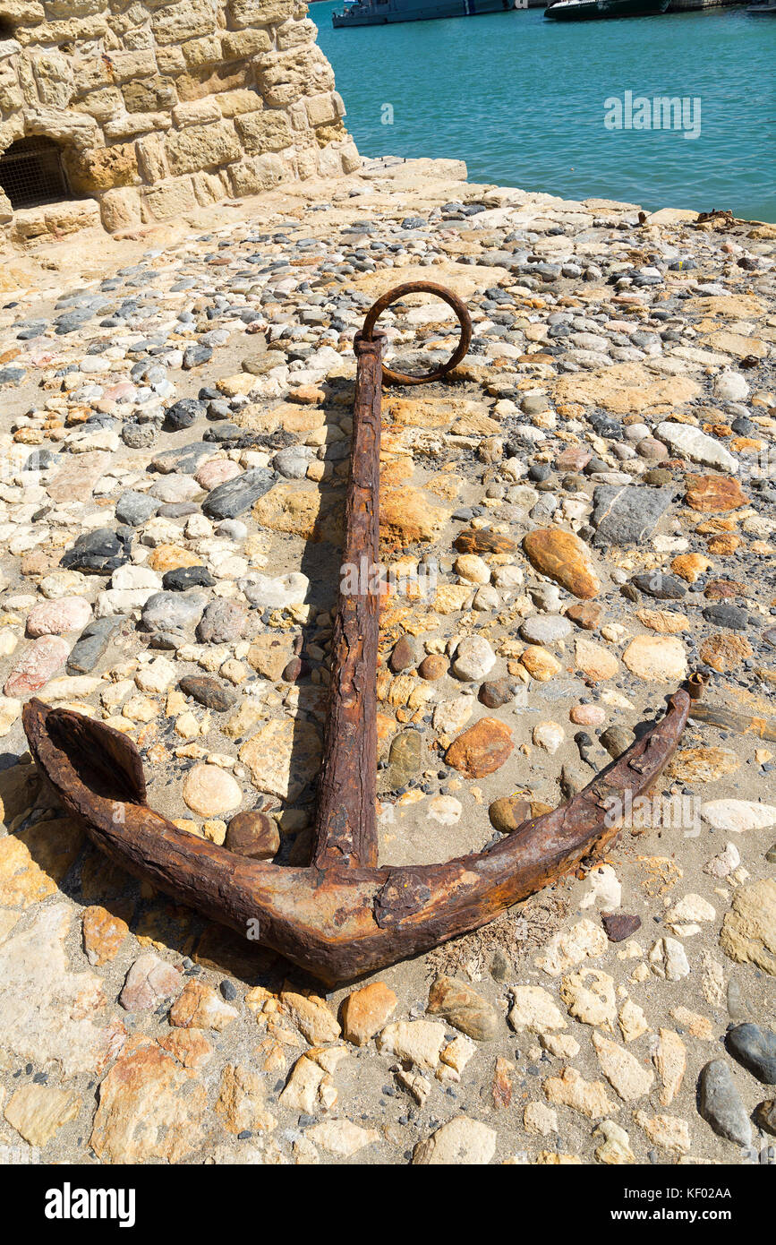 Old anchor is lying on the rocks near the port on the island of Crete ...