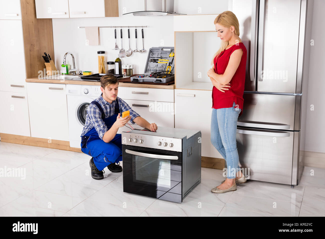 Male Worker Repairing Oven Using Multimeter With Young Woman Standing ...