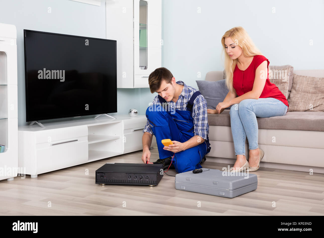Woman Sitting On Couch Looking At Male Technician Installing TV Set Top ...