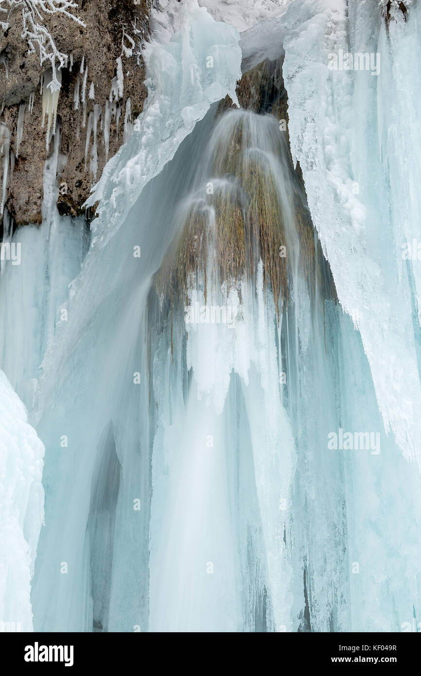Icicles hang from a frozen waterfall as water flows over a tufa dam ...