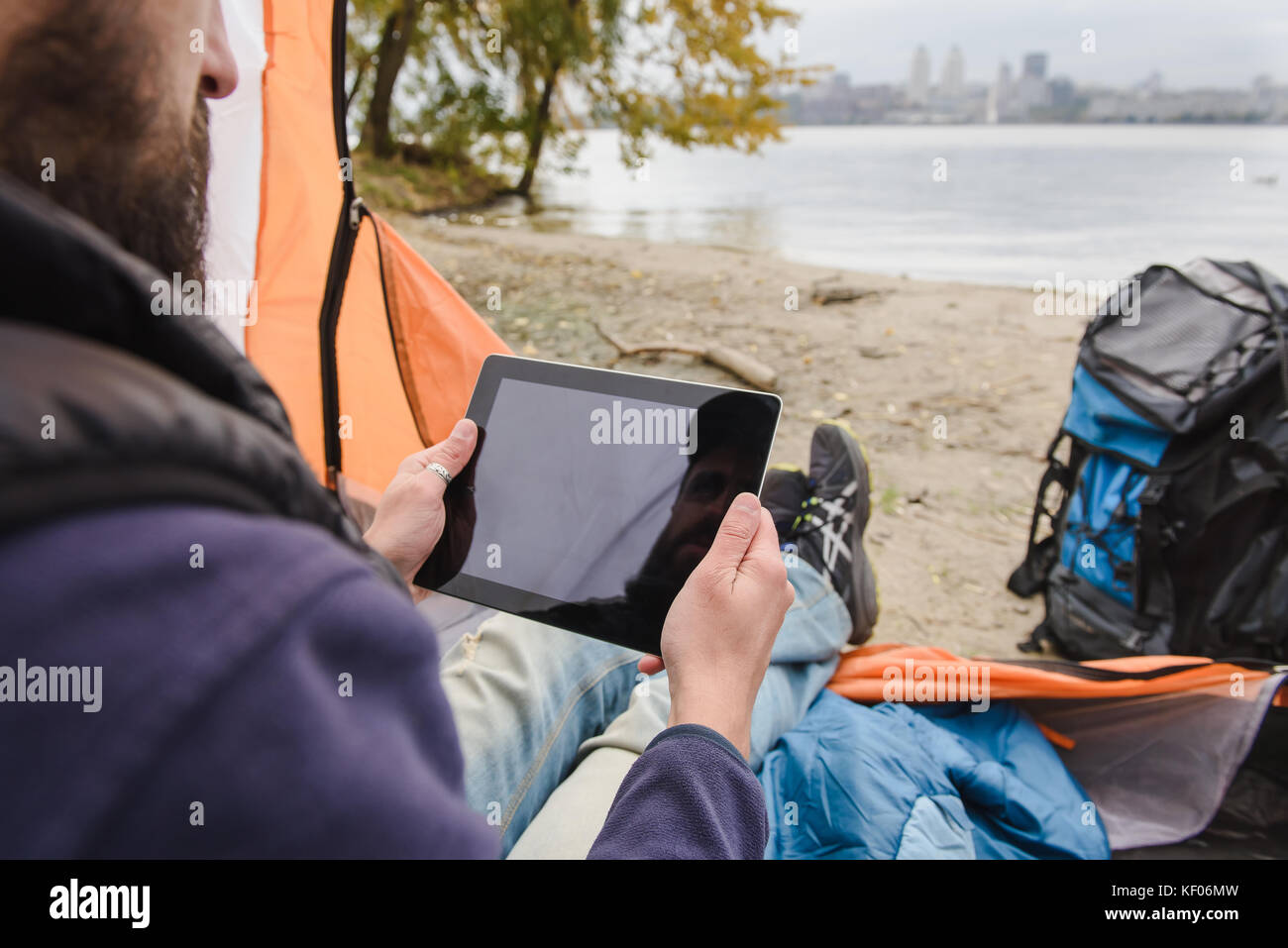 Man using digital tablet in camping tent. A backpack next to the tent ...