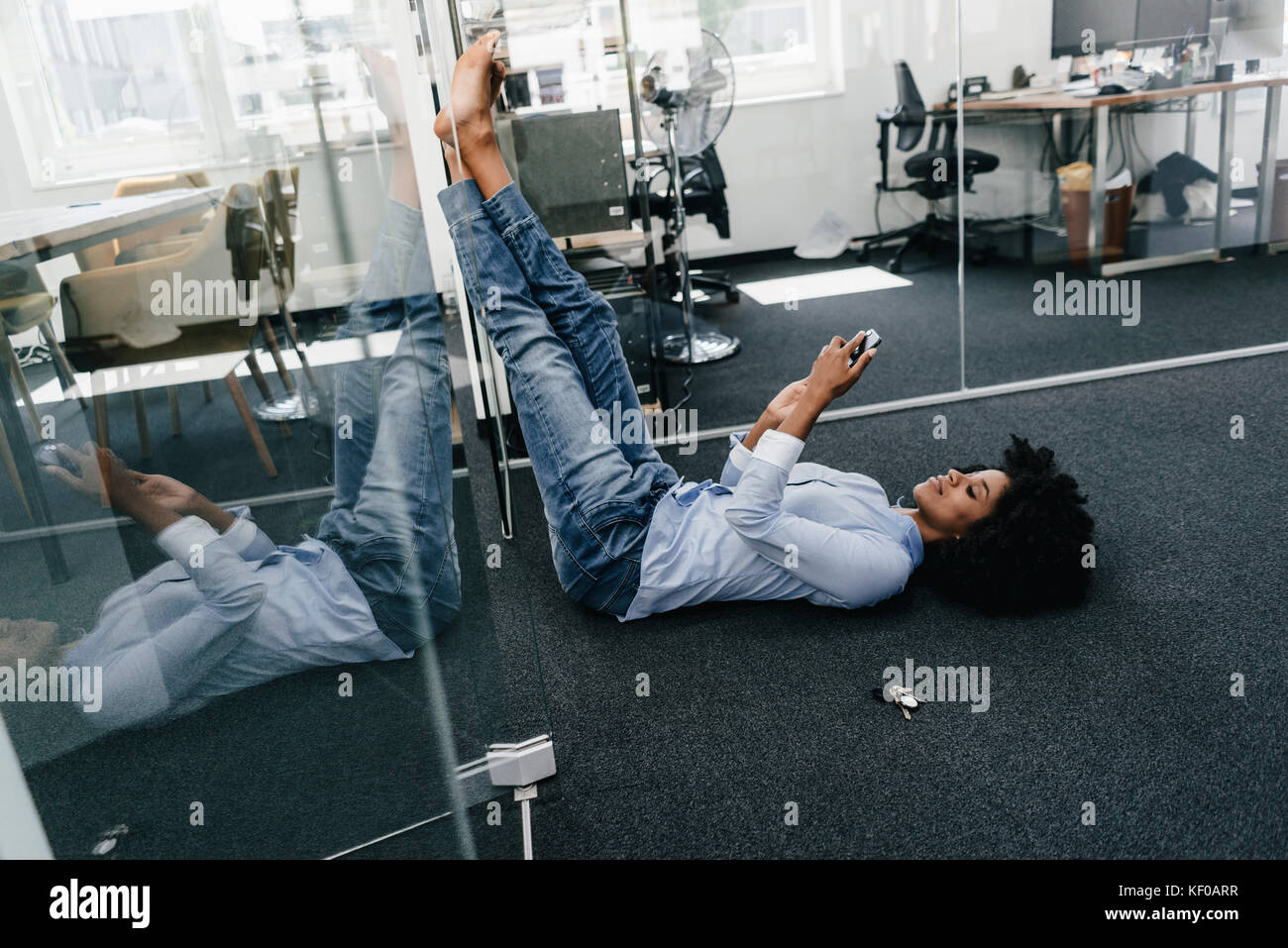 Young woman lying on the floor in office checking cell phone Stock ...