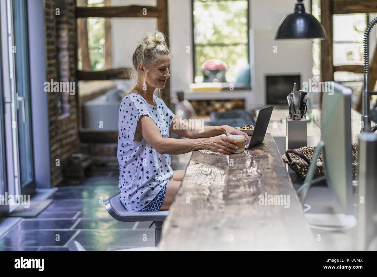 Woman sitting in kitchen, using laptop Stock Photo - Alamy