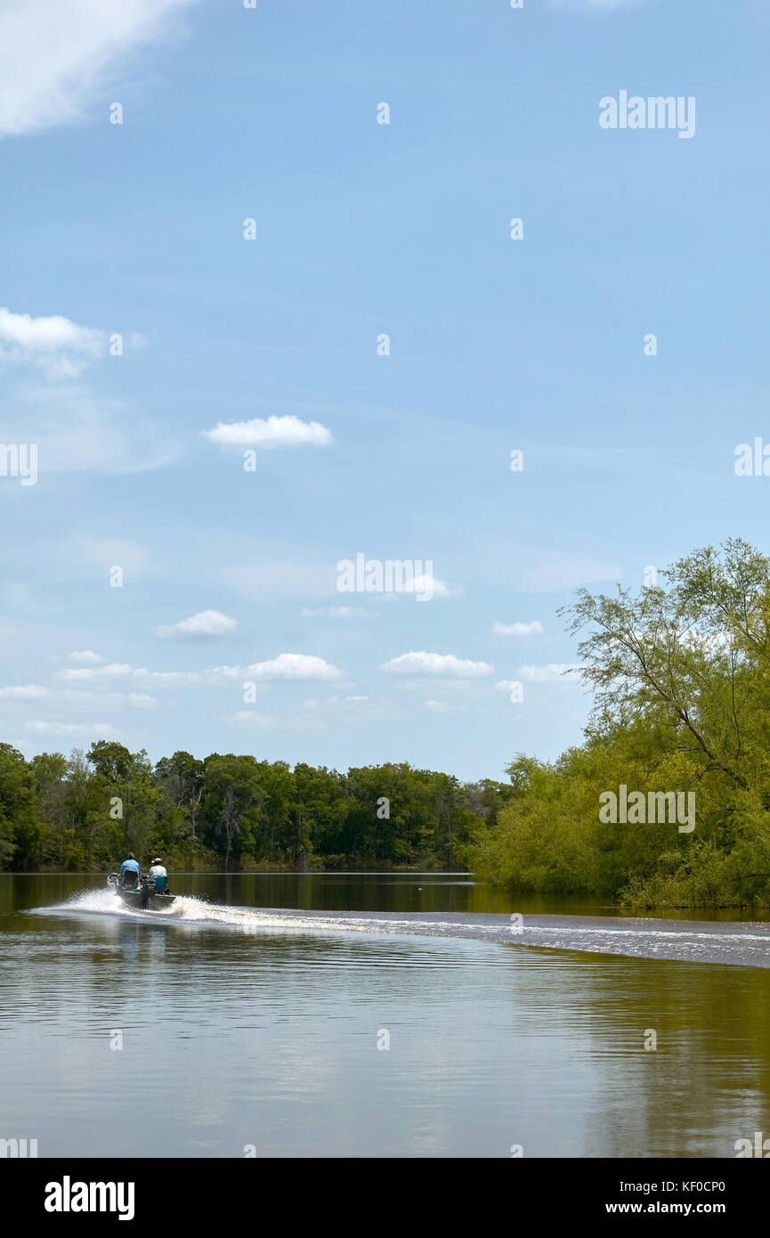 A boat driving on a scenic river leaves a wake on the calm water ...