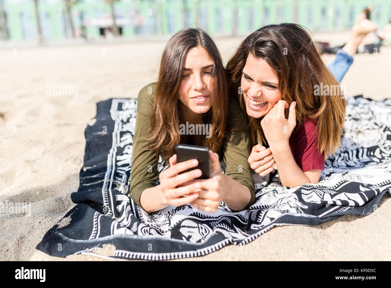 Two happy female friends using cell phone on the beach Stock Photo - Alamy