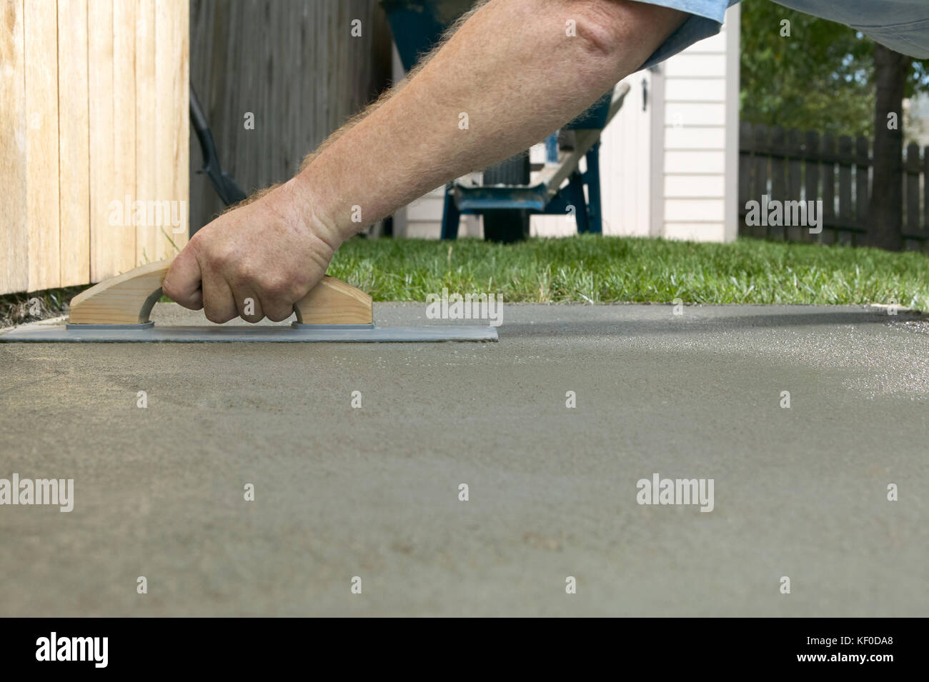 A person finishing wet cement with a concrete screed in a backyard, DIY ...