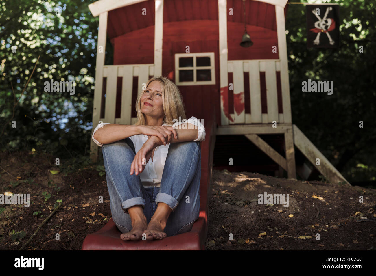 Mature woman sitting on slide in front of garden shed in the woods ...