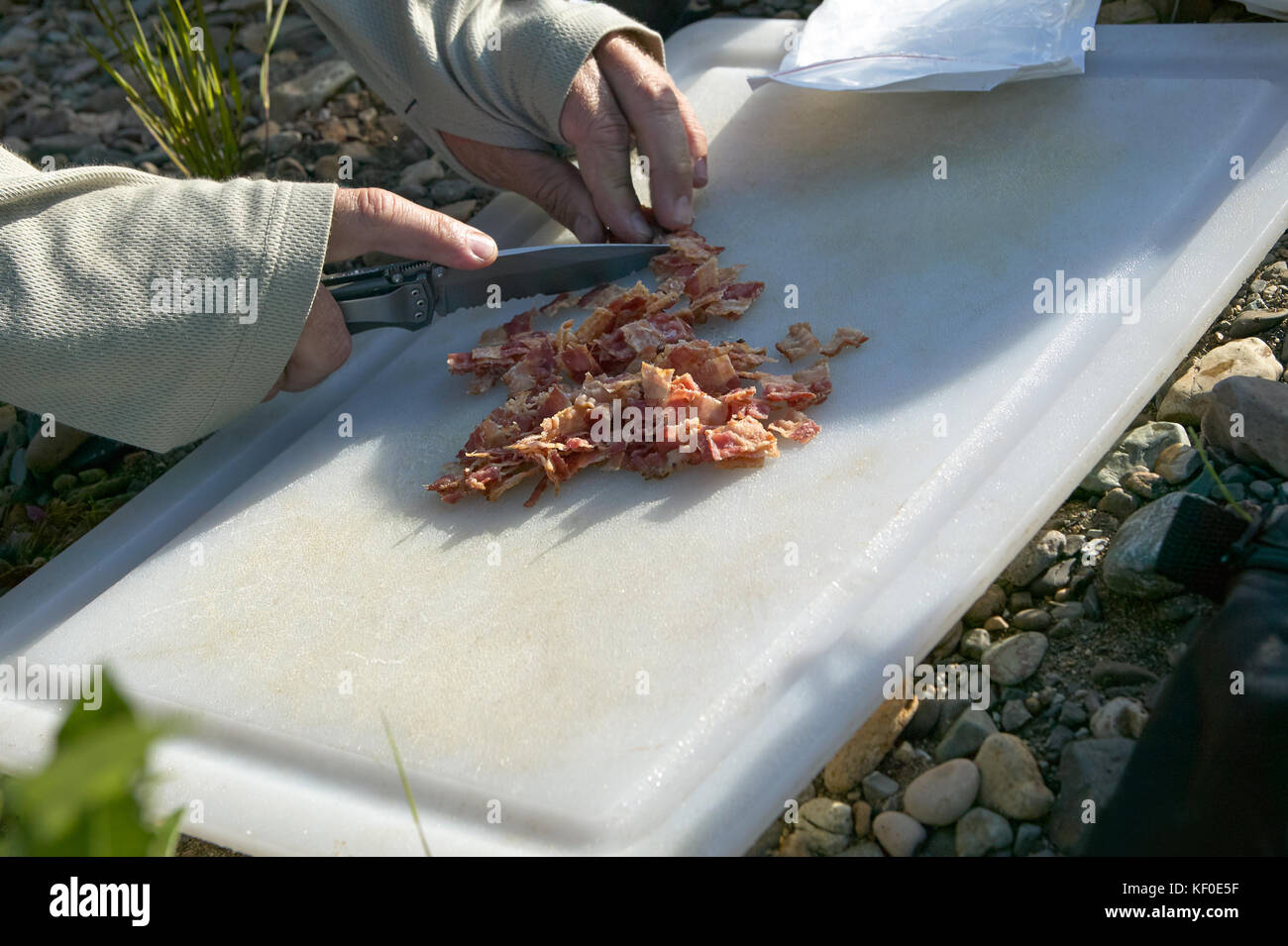 A close up of a person chopping bacon rations on a plastic chopping ...