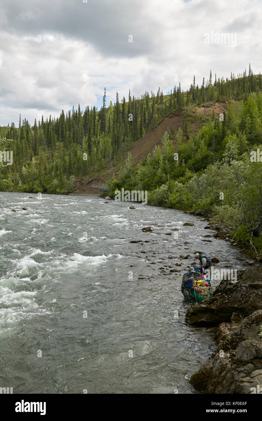 Two men beach their canoe beside turbulent, raging rapids on a wild ...