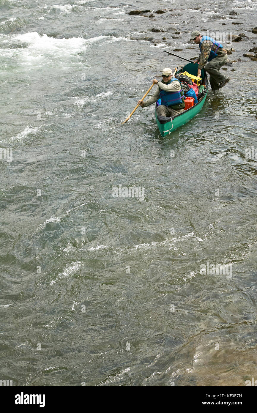 Two adventurers in a small canoe navigating shallow, wild river rapids ...