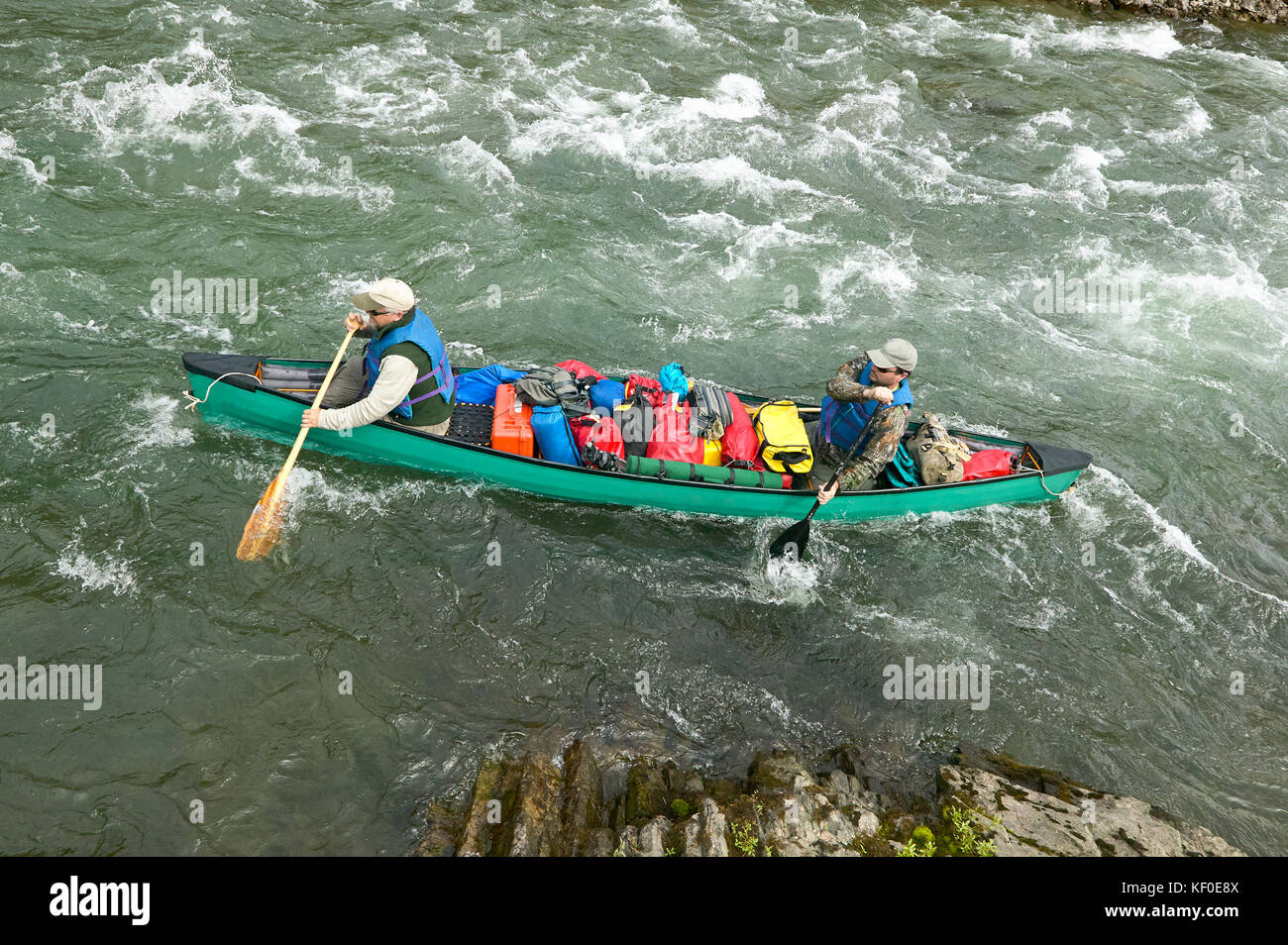 Two men navigate an overloaded canoe through rapids and rocks during an ...