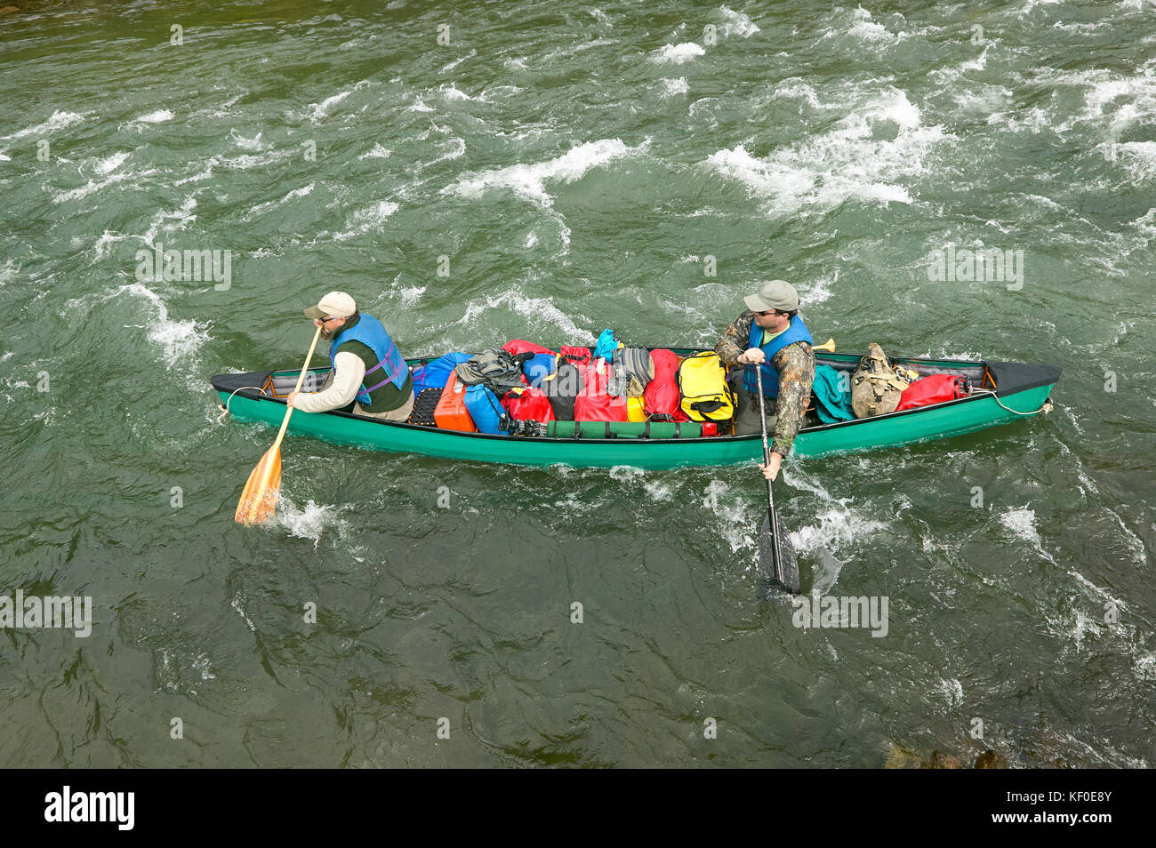 Two men navigate an overloaded canoe through rushing rapids during an ...
