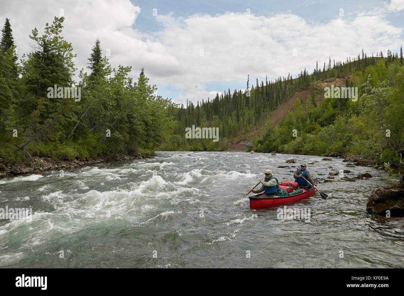 Two men navigate a canoe through rushing rapids during an adventure on ...