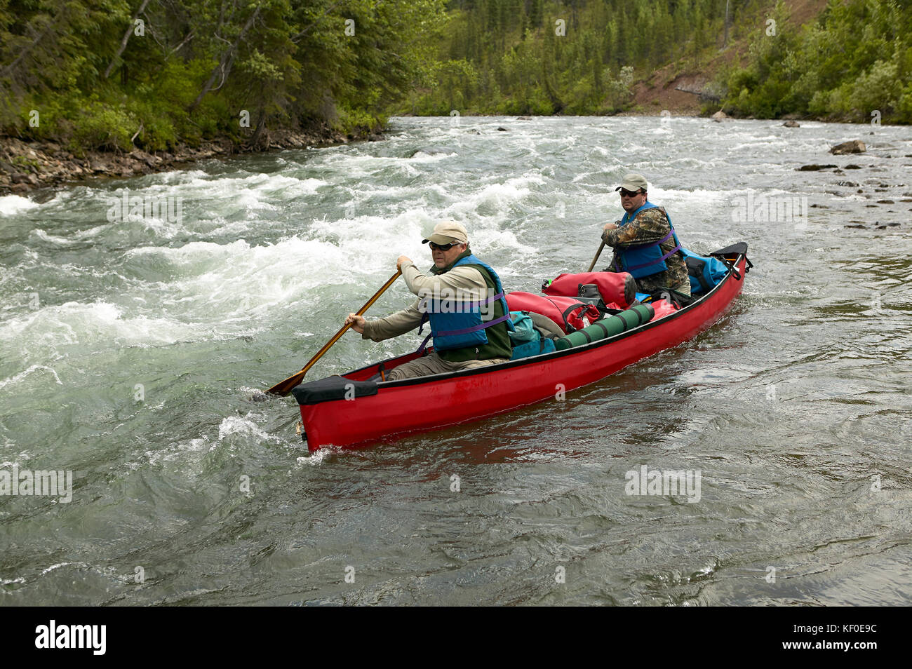 Two men navigate a canoe through rushing rapids during an adventure on ...