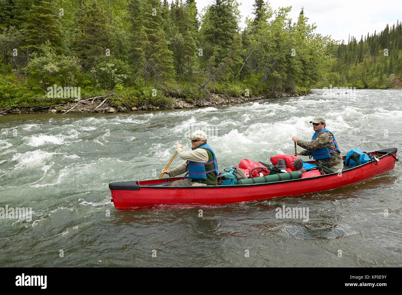 Two men navigate a canoe through rushing rapids during an adventure on ...