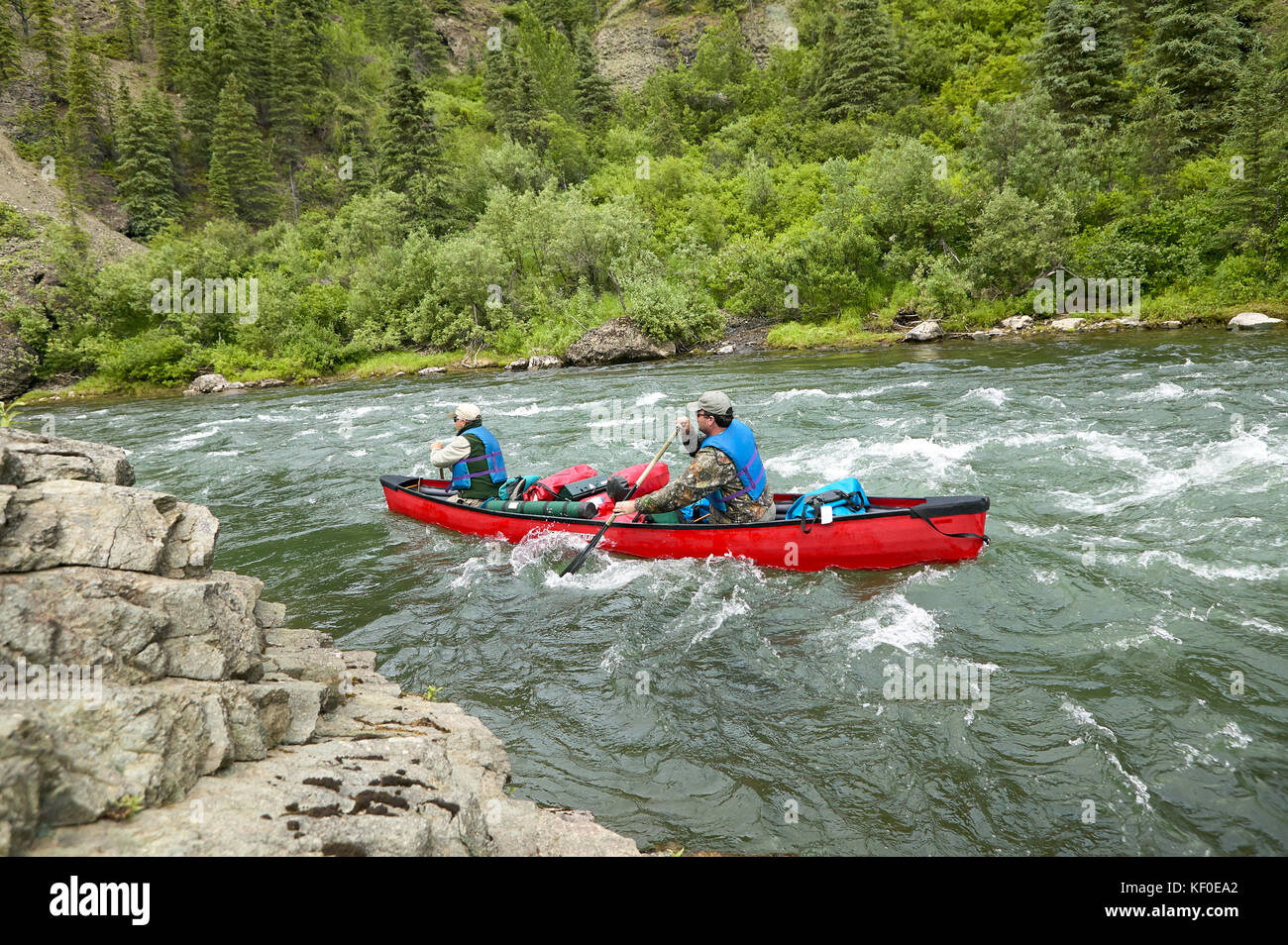 Two men navigate a canoe through rushing, turbulent, rough rapids ...