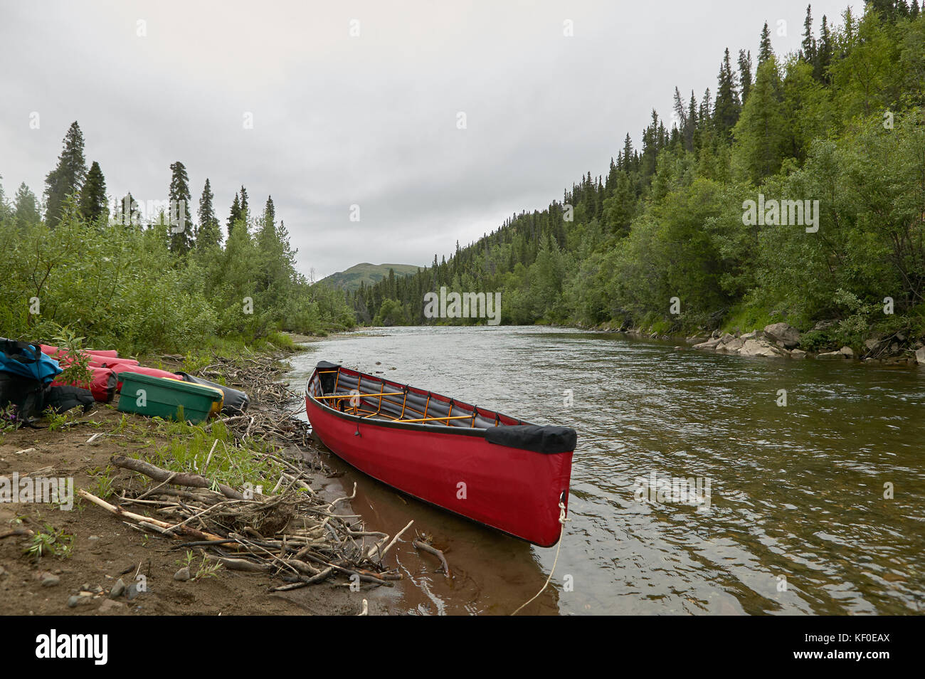 A beached red, inflatable canoe on an Alaskan river with wet gear and ...