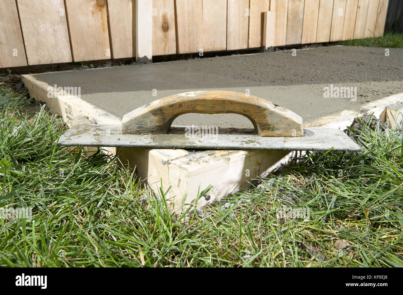 A close up of a wooden, cement screed finishing tool on a wet concrete ...