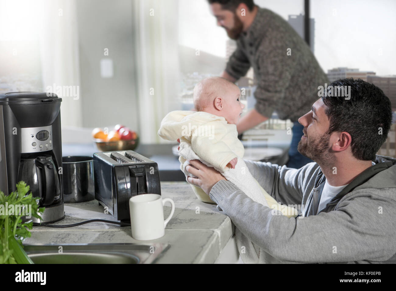 Two men with baby in kitchen Stock Photo - Alamy