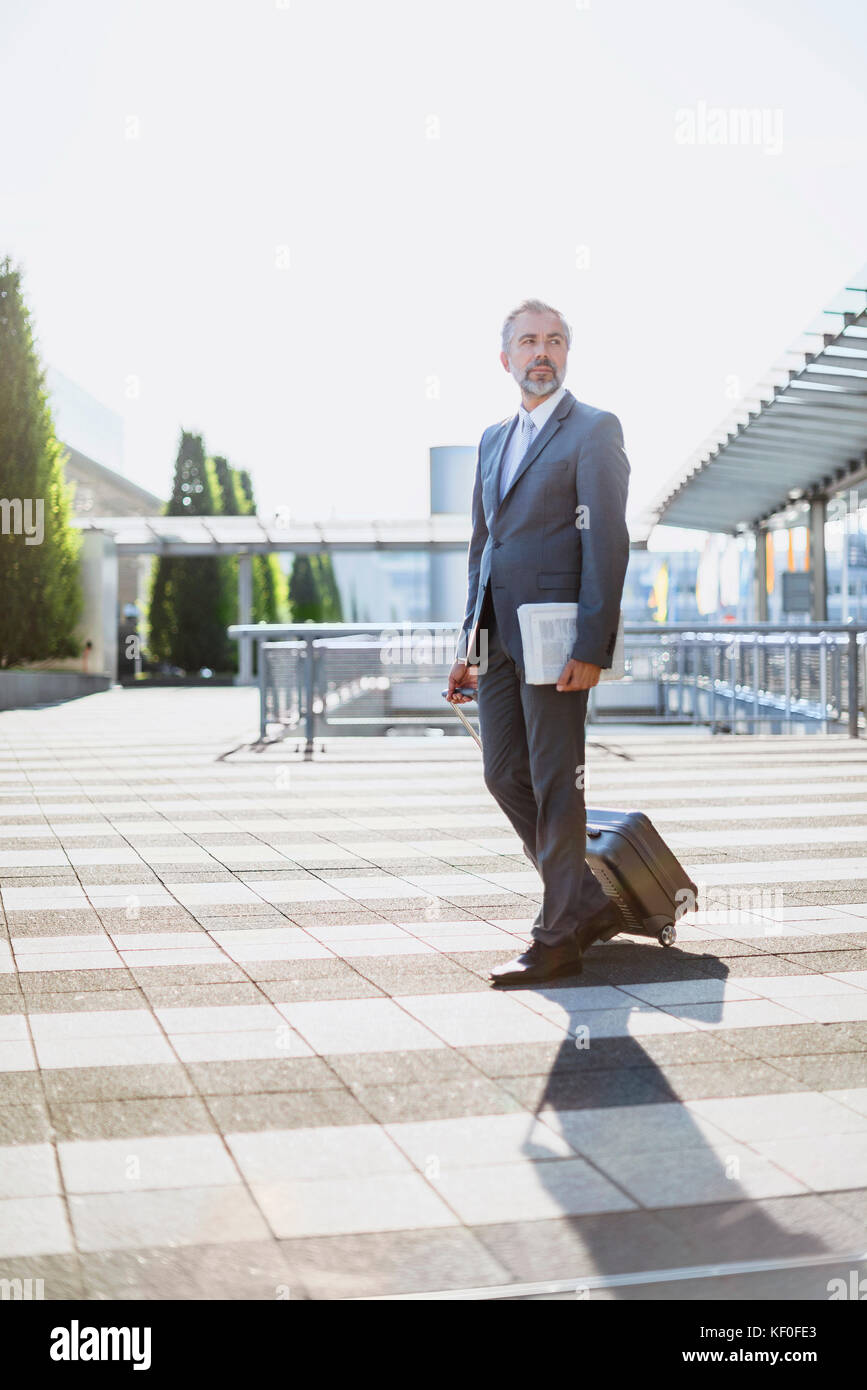 Businessman pulling rolling suitcase outdoors Stock Photo - Alamy