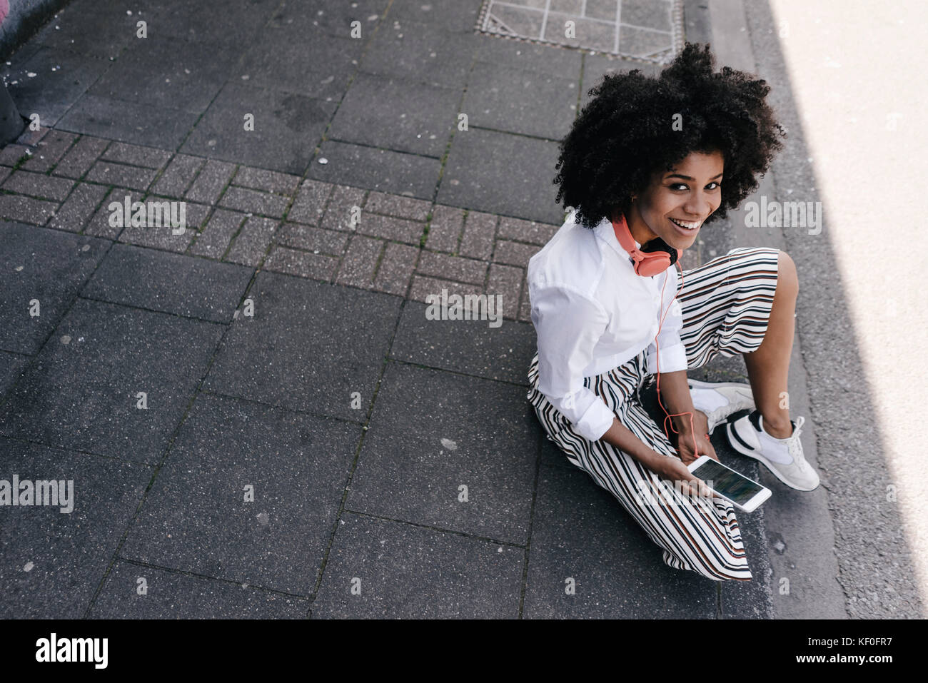Smiling young woman sitting on pavement Stock Photo - Alamy