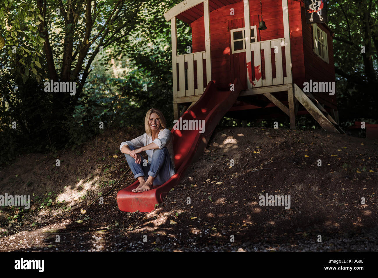 Mature woman sitting on slide in front of garden shed in the woods ...