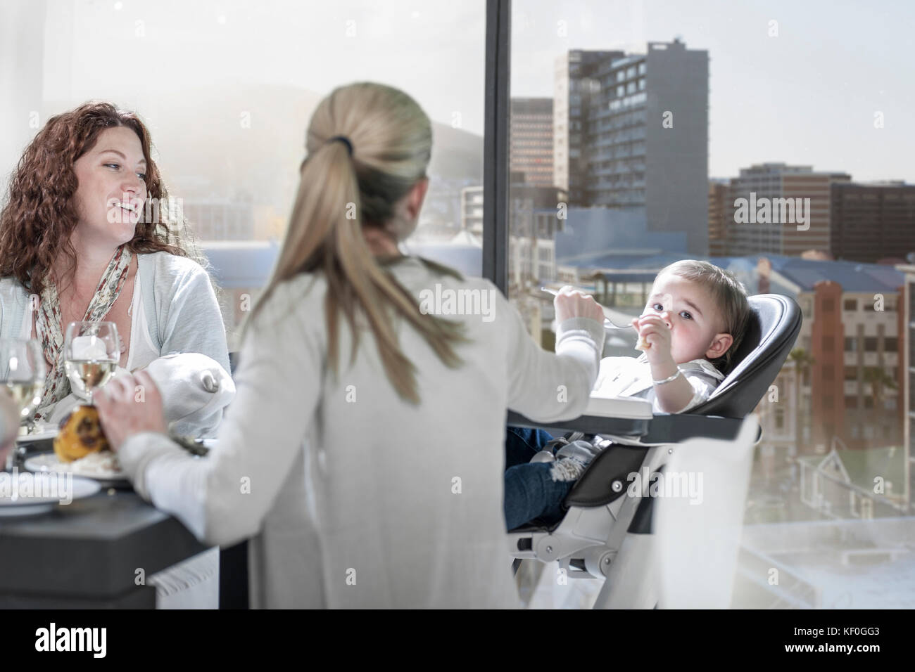 Mother with friend feeding baby at dining table Stock Photo - Alamy
